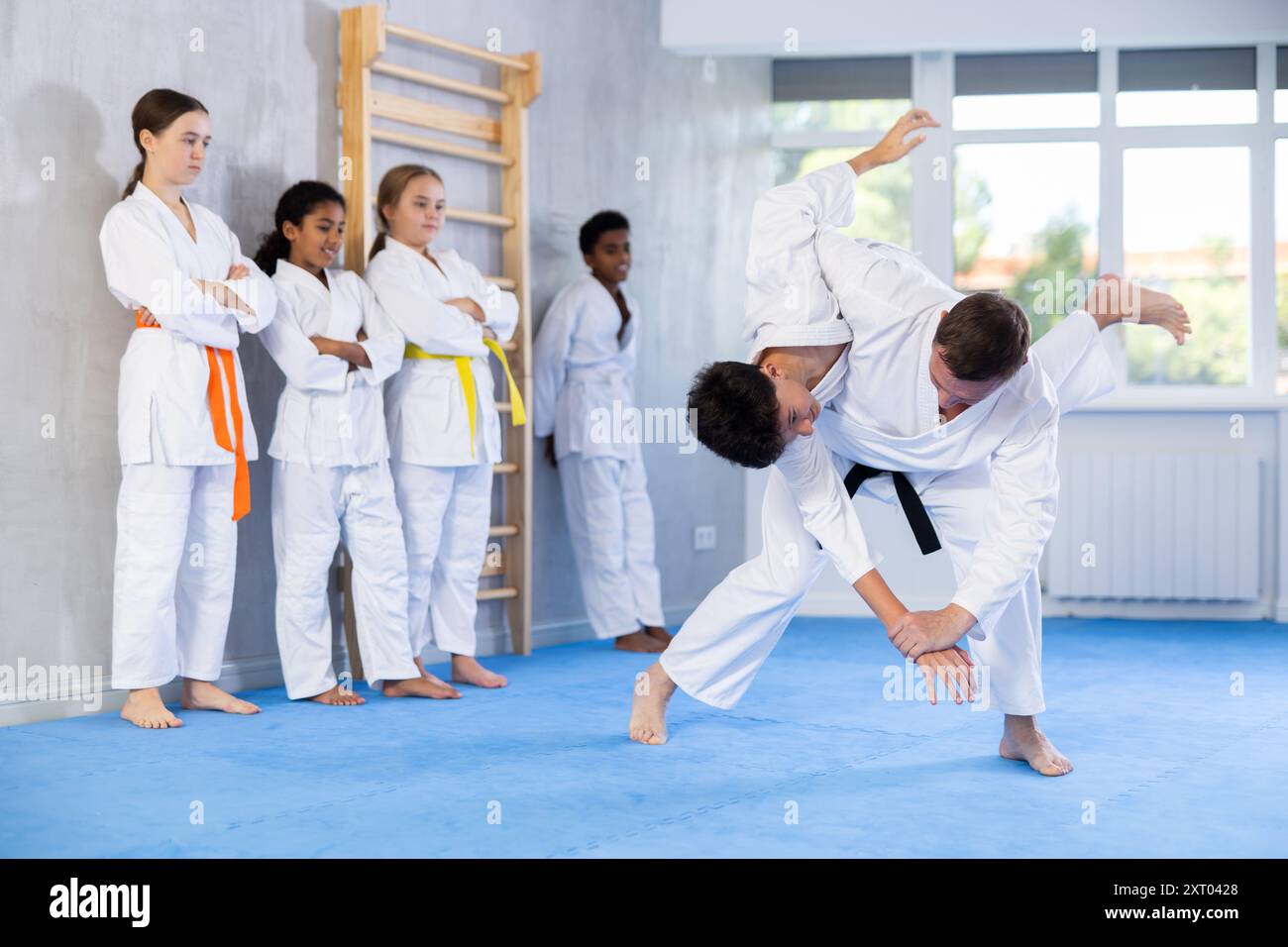 Judo coach shows fighting techniques in sparring with a boy for group ...