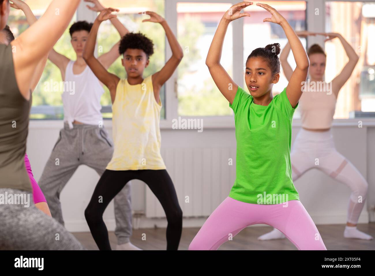 Thin teenage girl practicing plie position of ballet standing in row ...