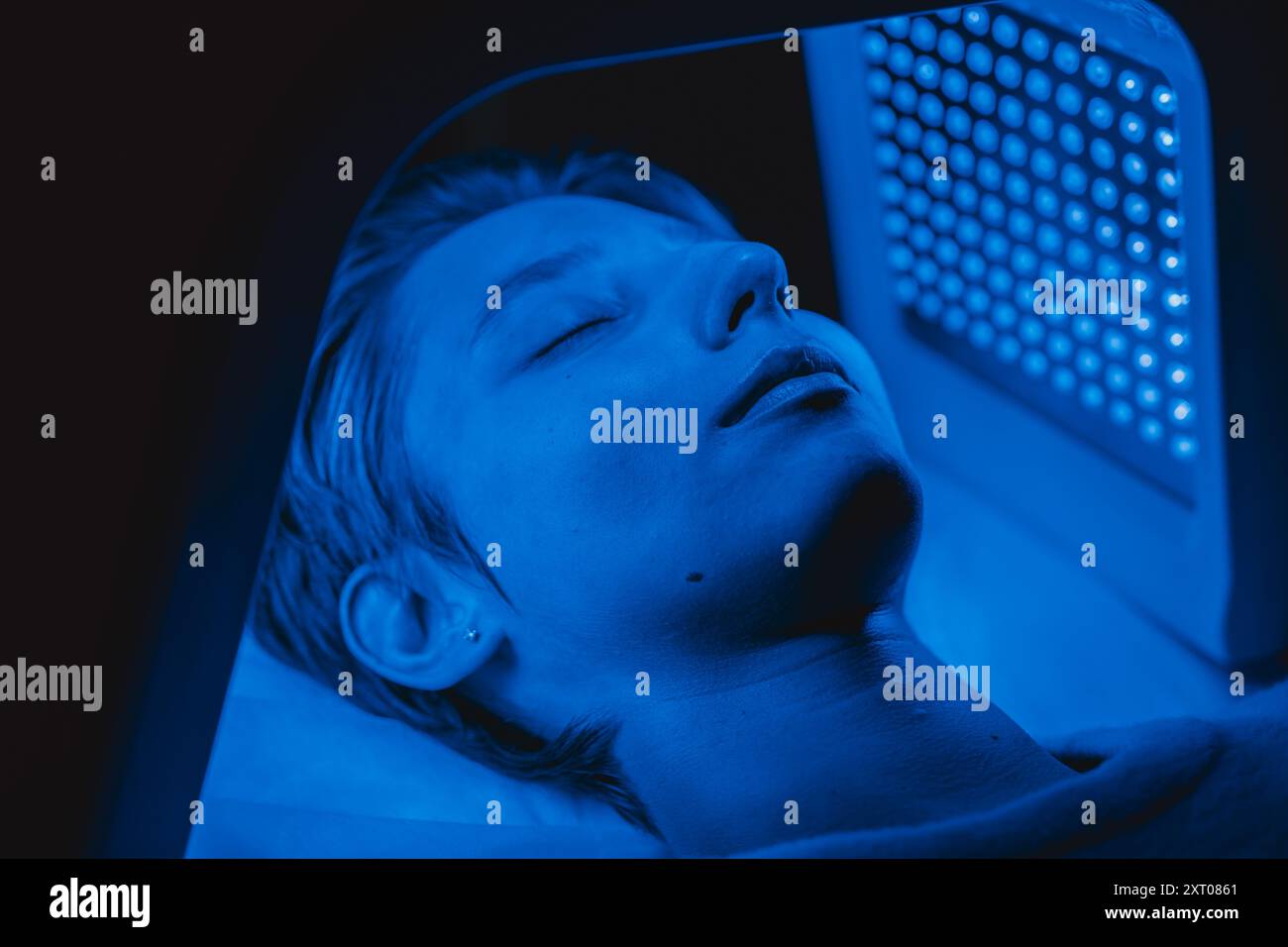 A young woman is treating the skin of her face with the help of LED ...