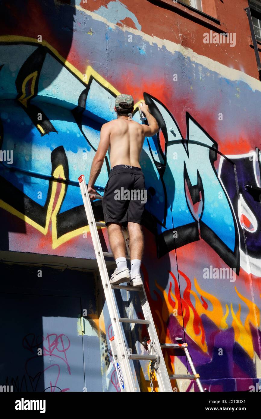 Male graffiti artist spray painting a mural on the side of a building ...