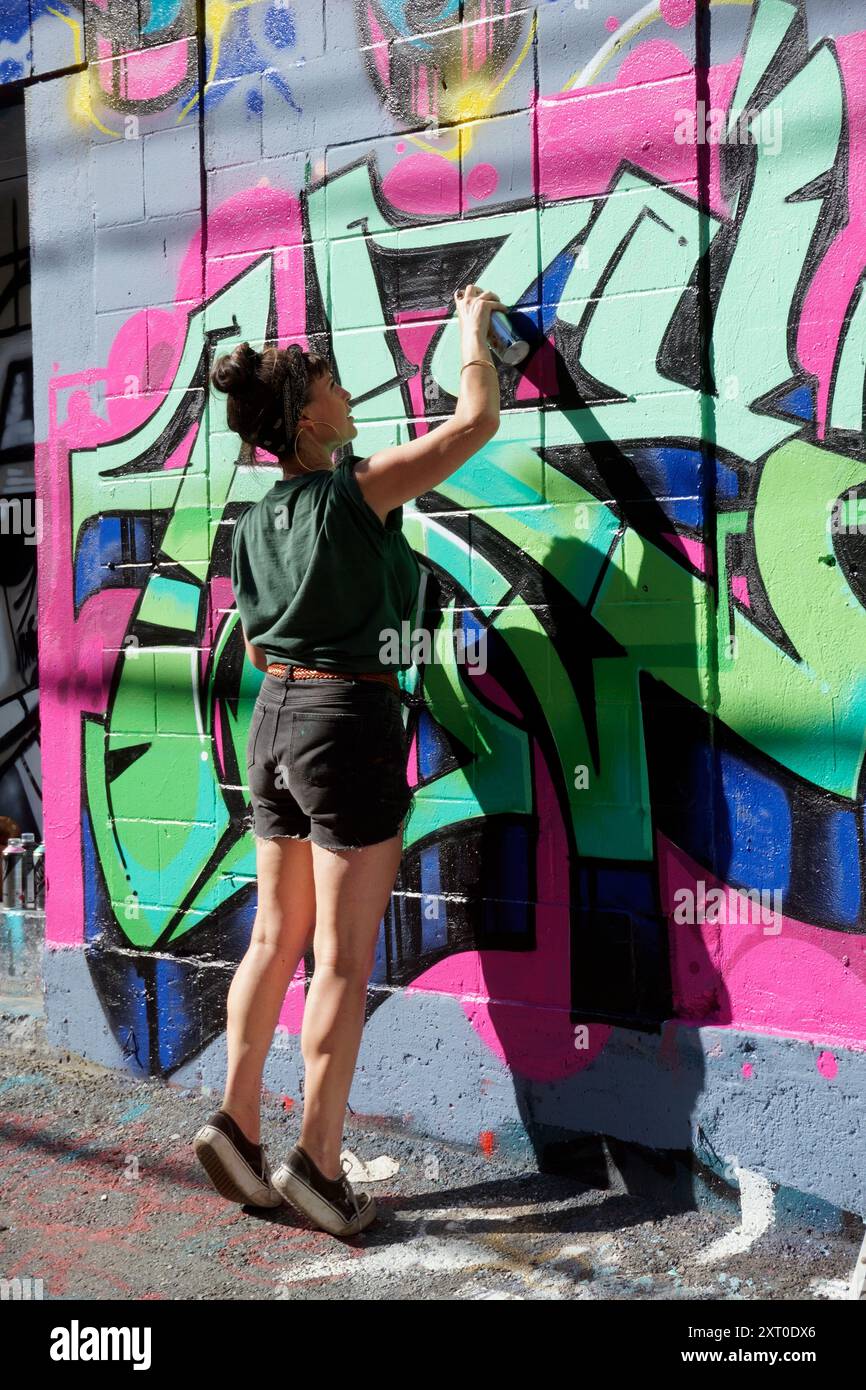 Female graffiti artist spray painting a mural on the side of a building ...