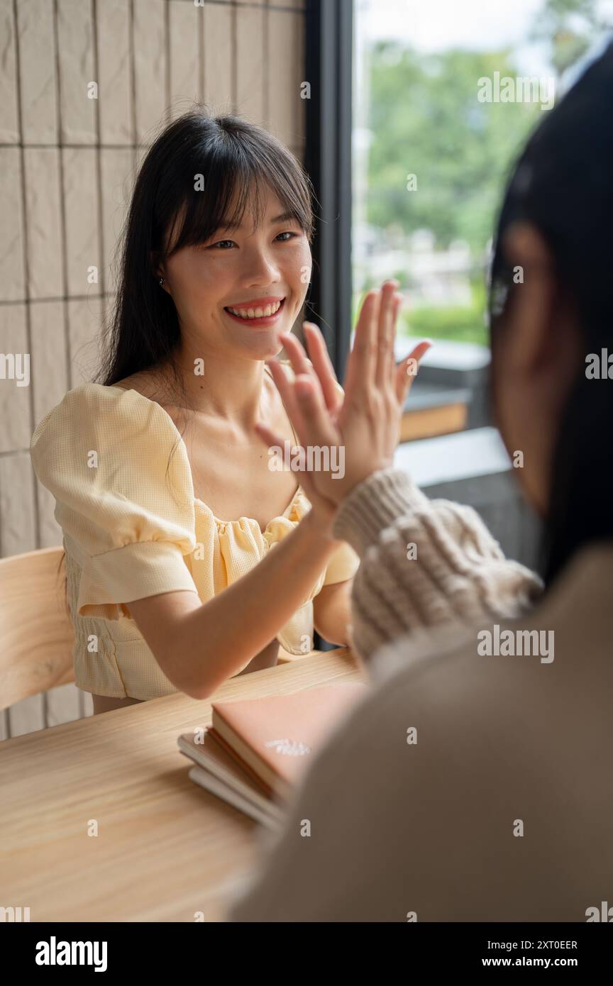 A beautiful, cheerful Asian woman is giving a high five to her friend ...