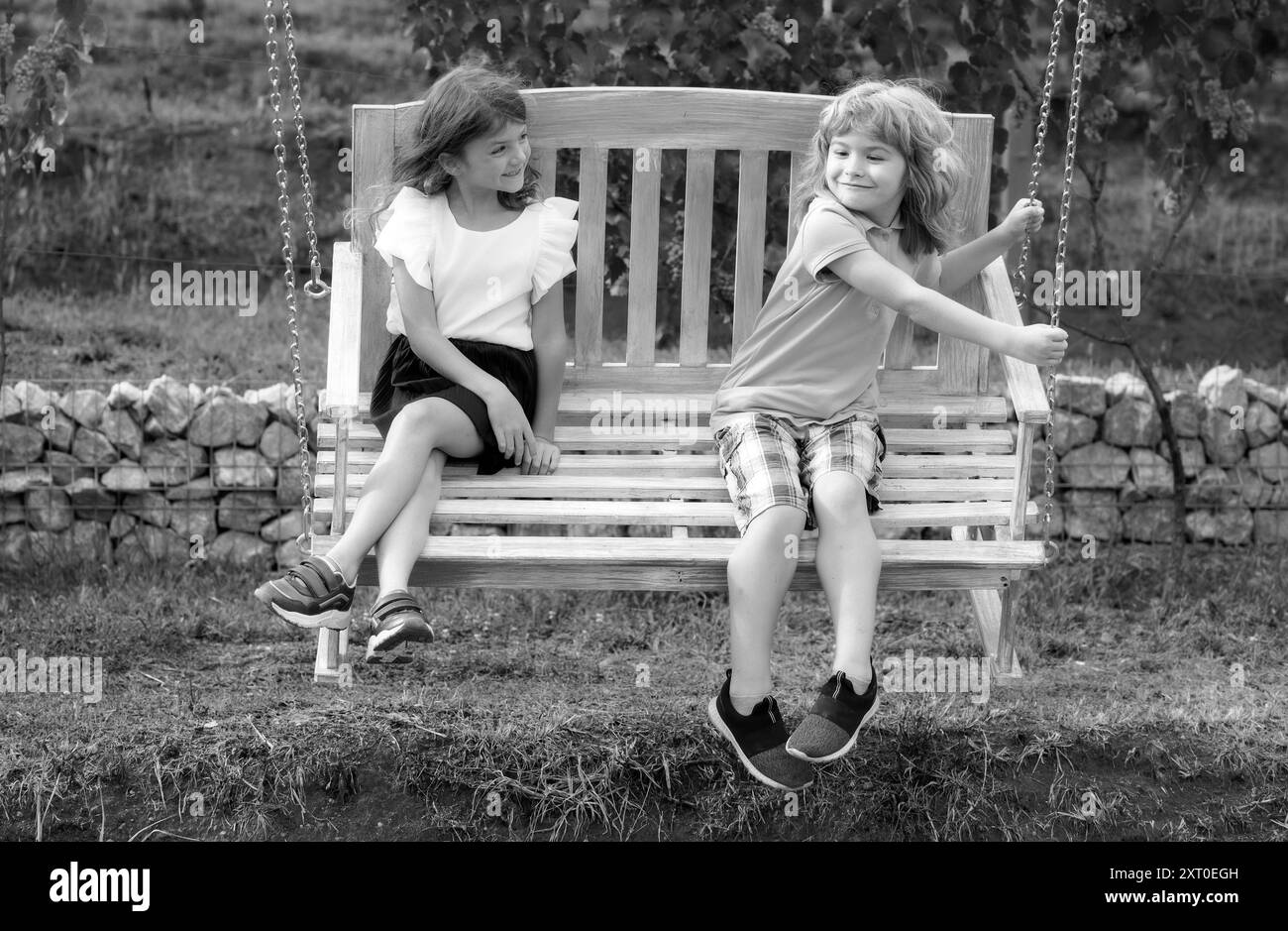 Brother and sister playing, swinging on swing in spring park outdoors ...