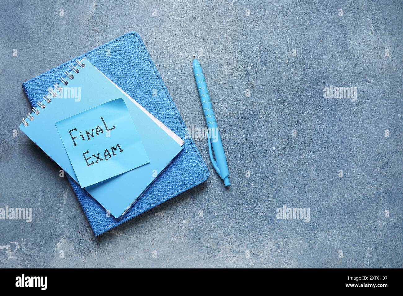 Sticky note with text FINAL EXAM, notebooks and pen on grunge blue ...