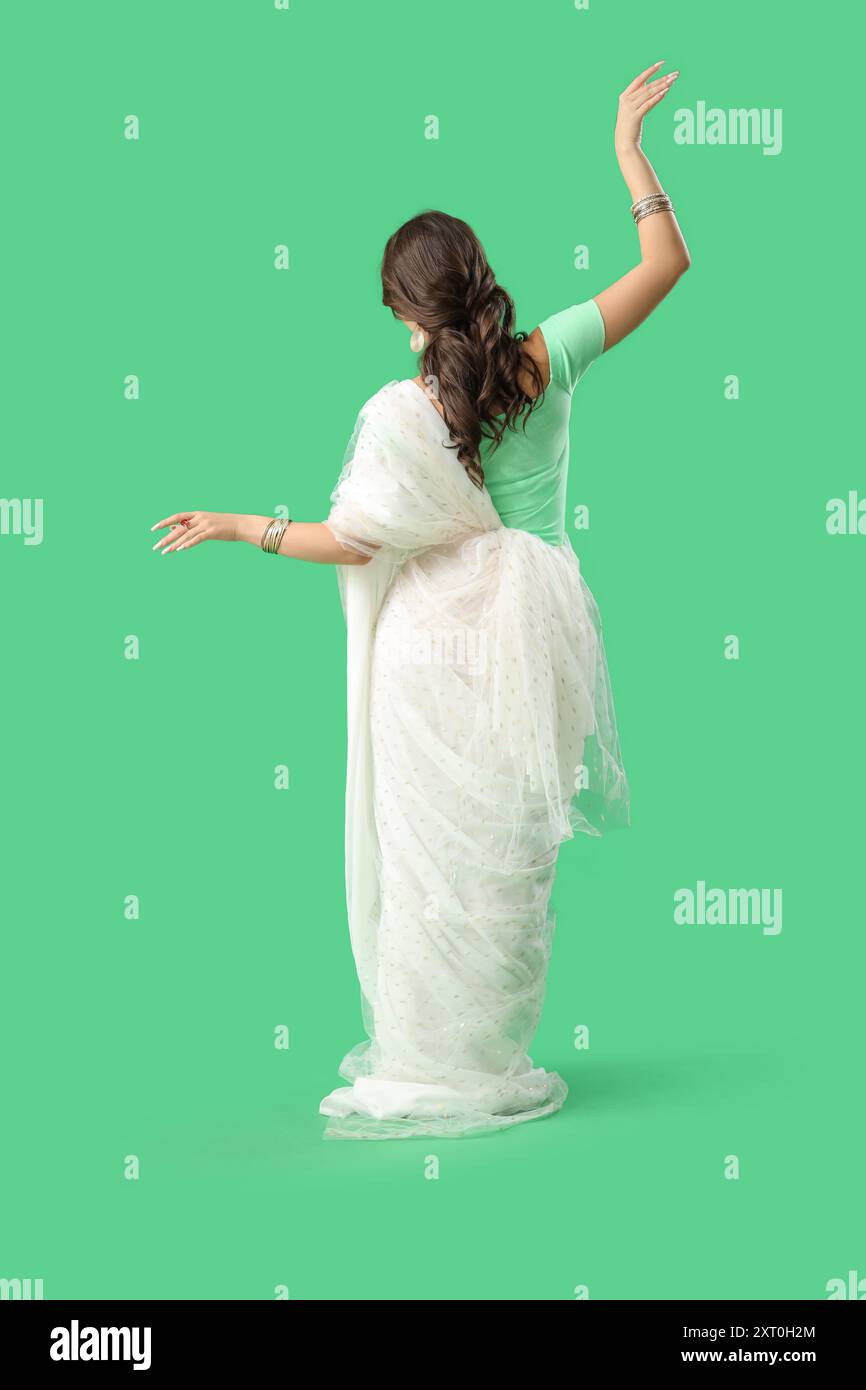 Beautiful young Indian woman in sari on green background, back view ...