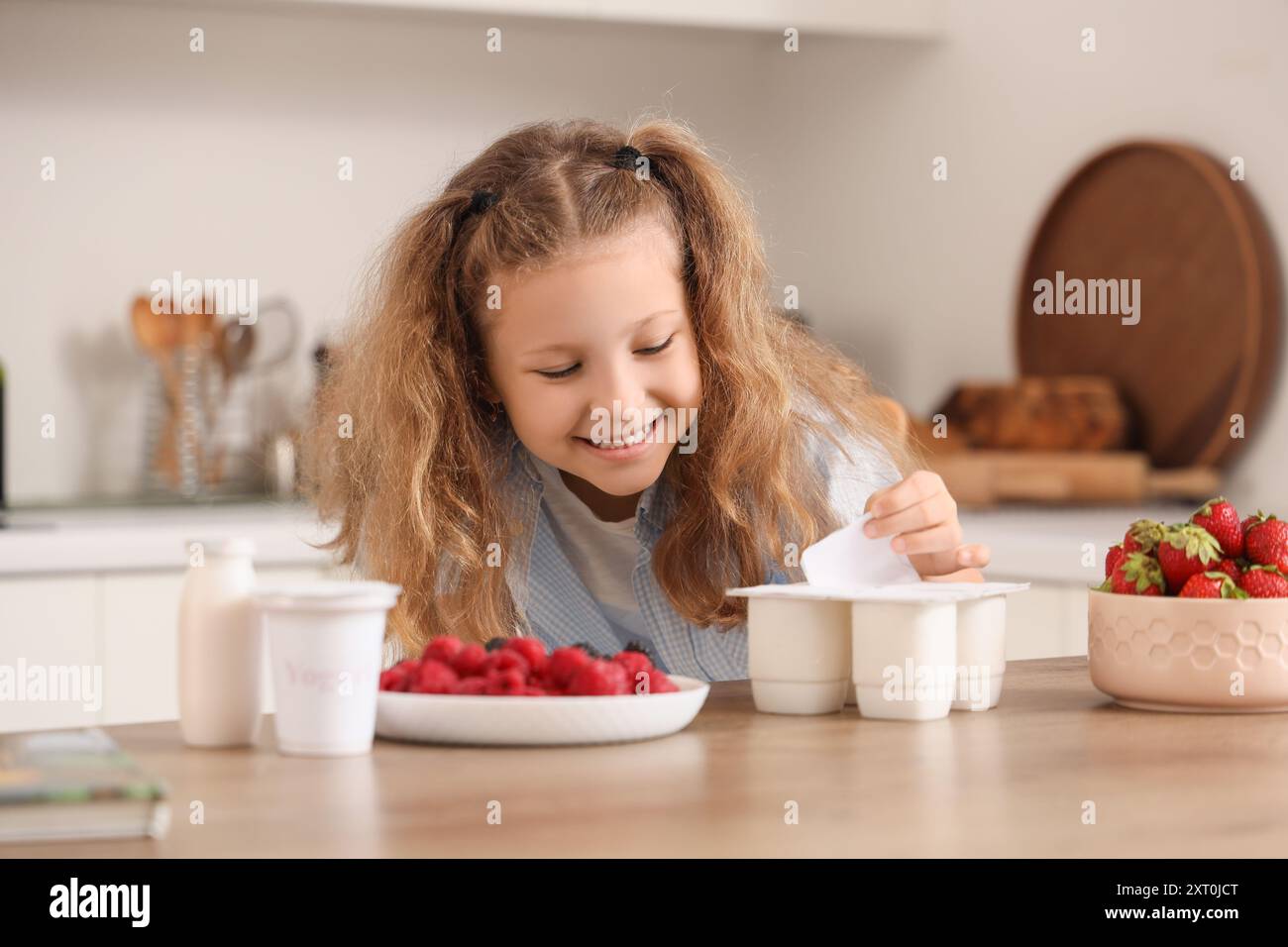 Happy little girl opening yogurt packs in kitchen Stock Photo - Alamy