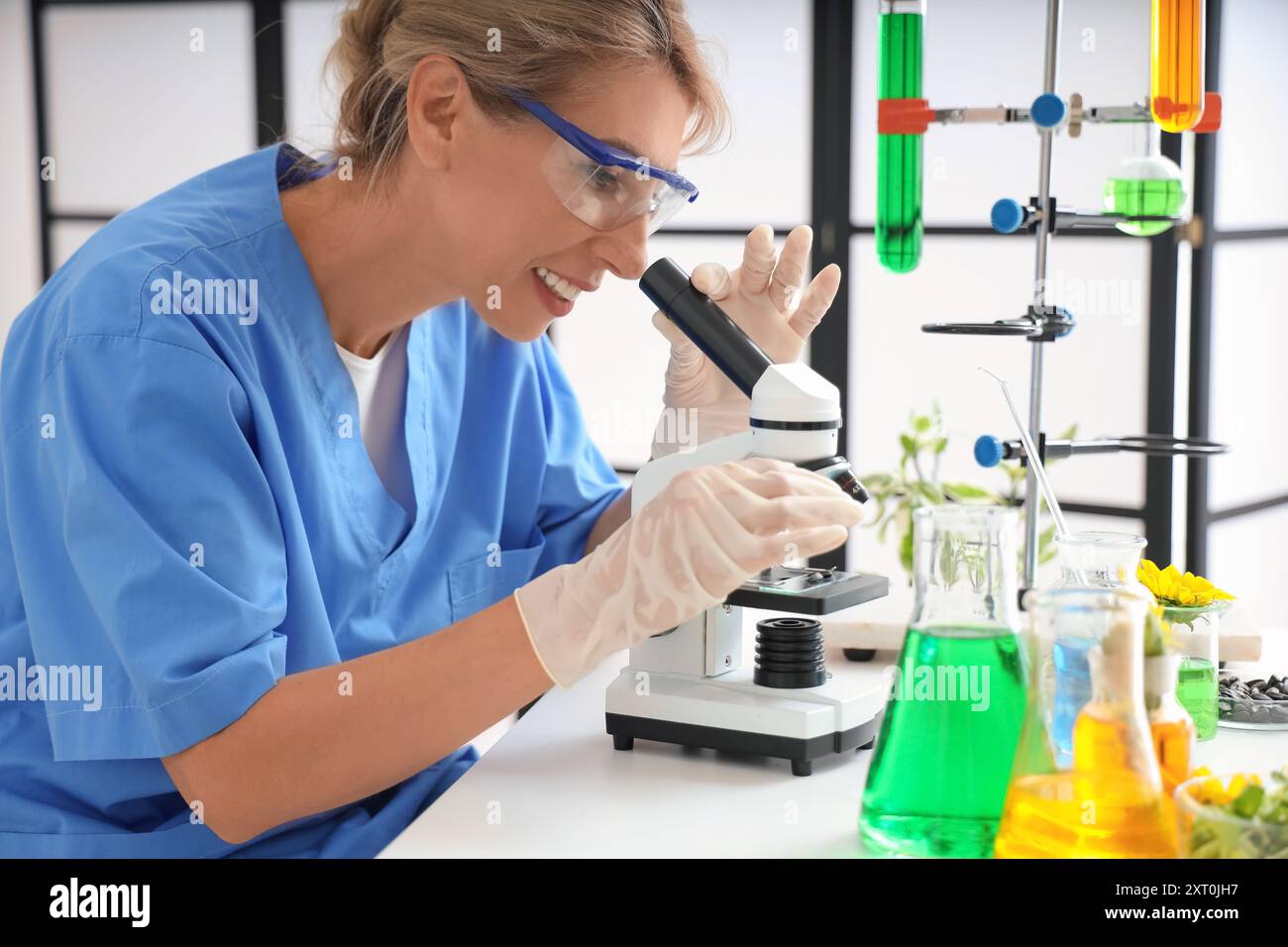 Happy female scientist with flasks of samples and microscope testing ...
