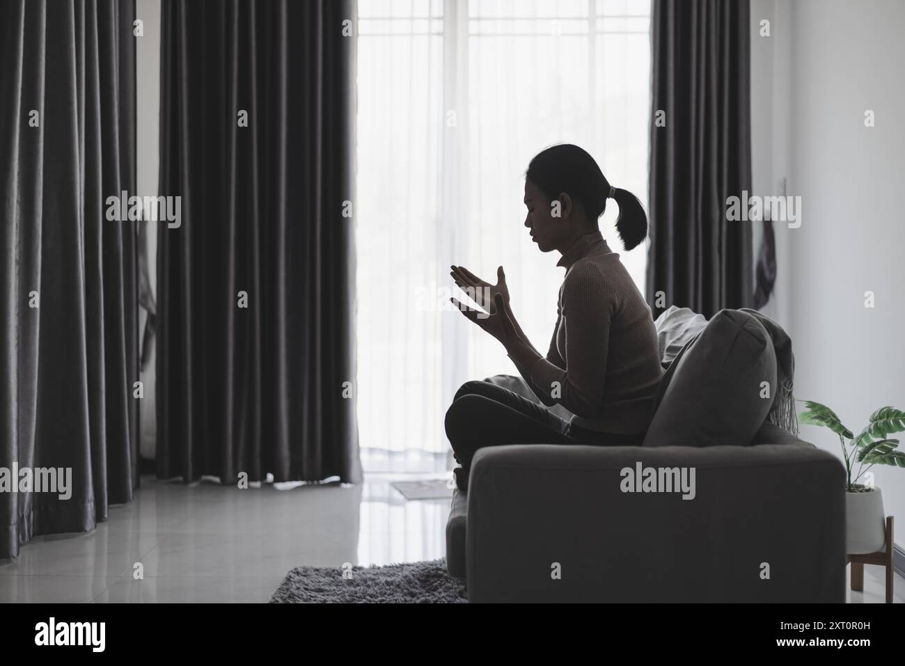 A woman who is a person of deep faith in God, praying on the sofa at ...