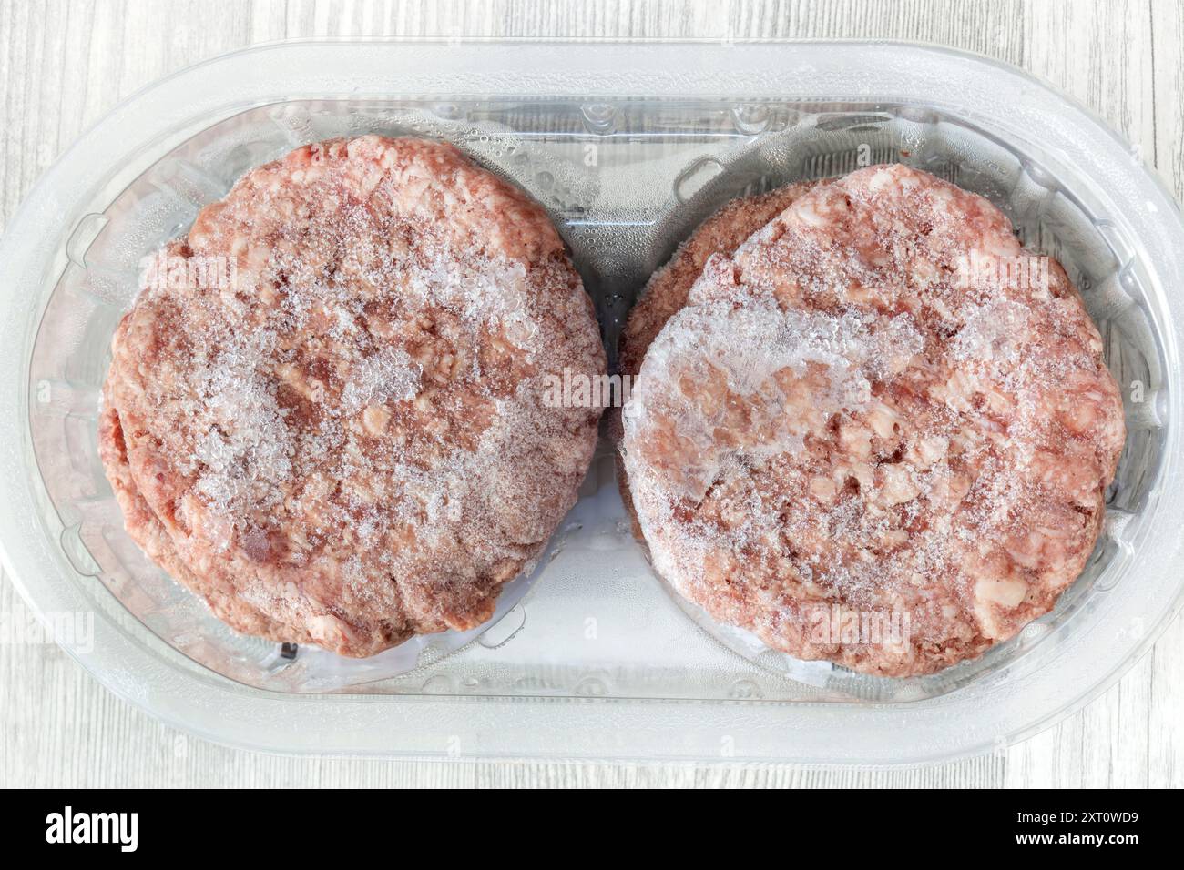 Frozen beef burgers in plastic tray packaging thawing. On a grey wood ...