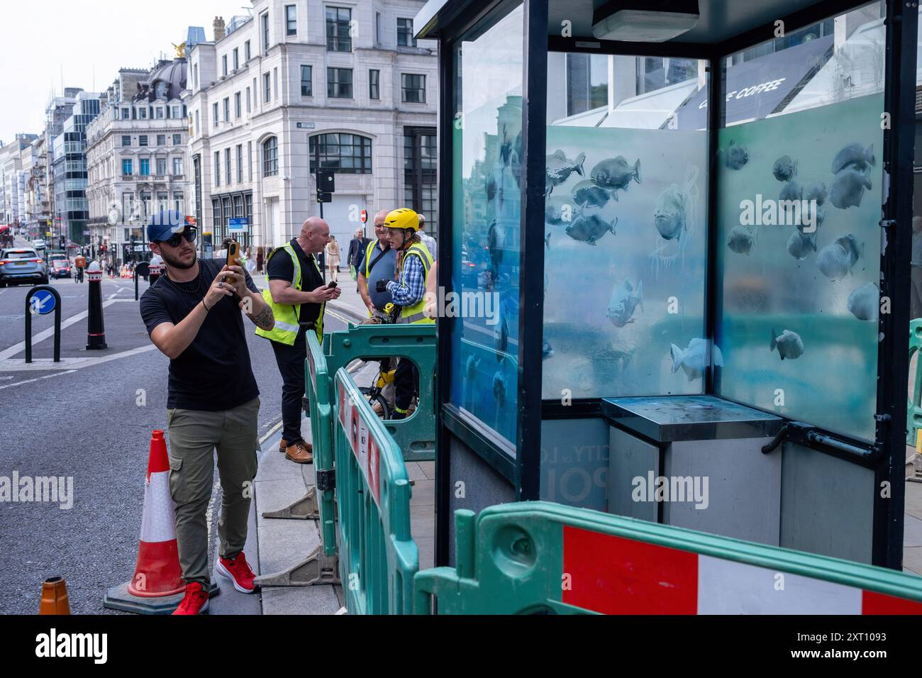 A man stands in the road to take a photograph of a piece of art using ...