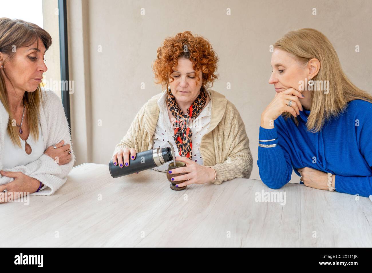 Three mid-adult women engage in a quiet, intimate conversation around a ...