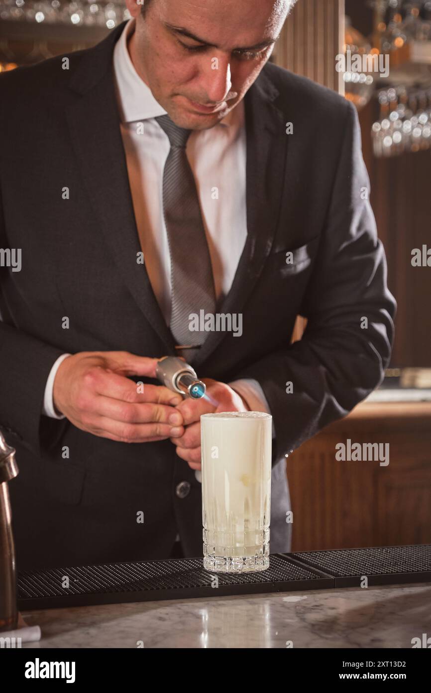 Concentrated male bartender in black suit using culinary torch on ...