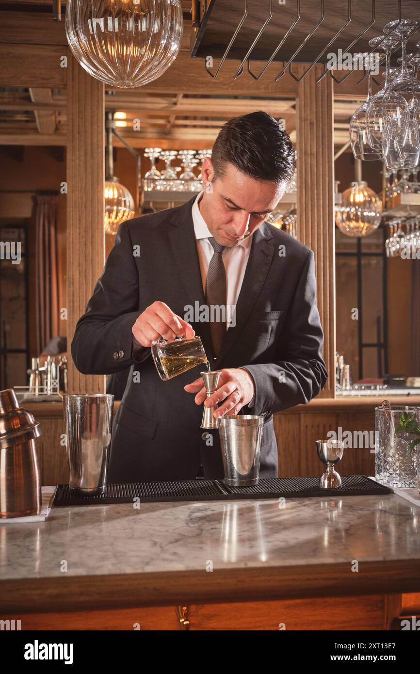 Male bartender in black suit pouring alcohol from flask in measuring ...