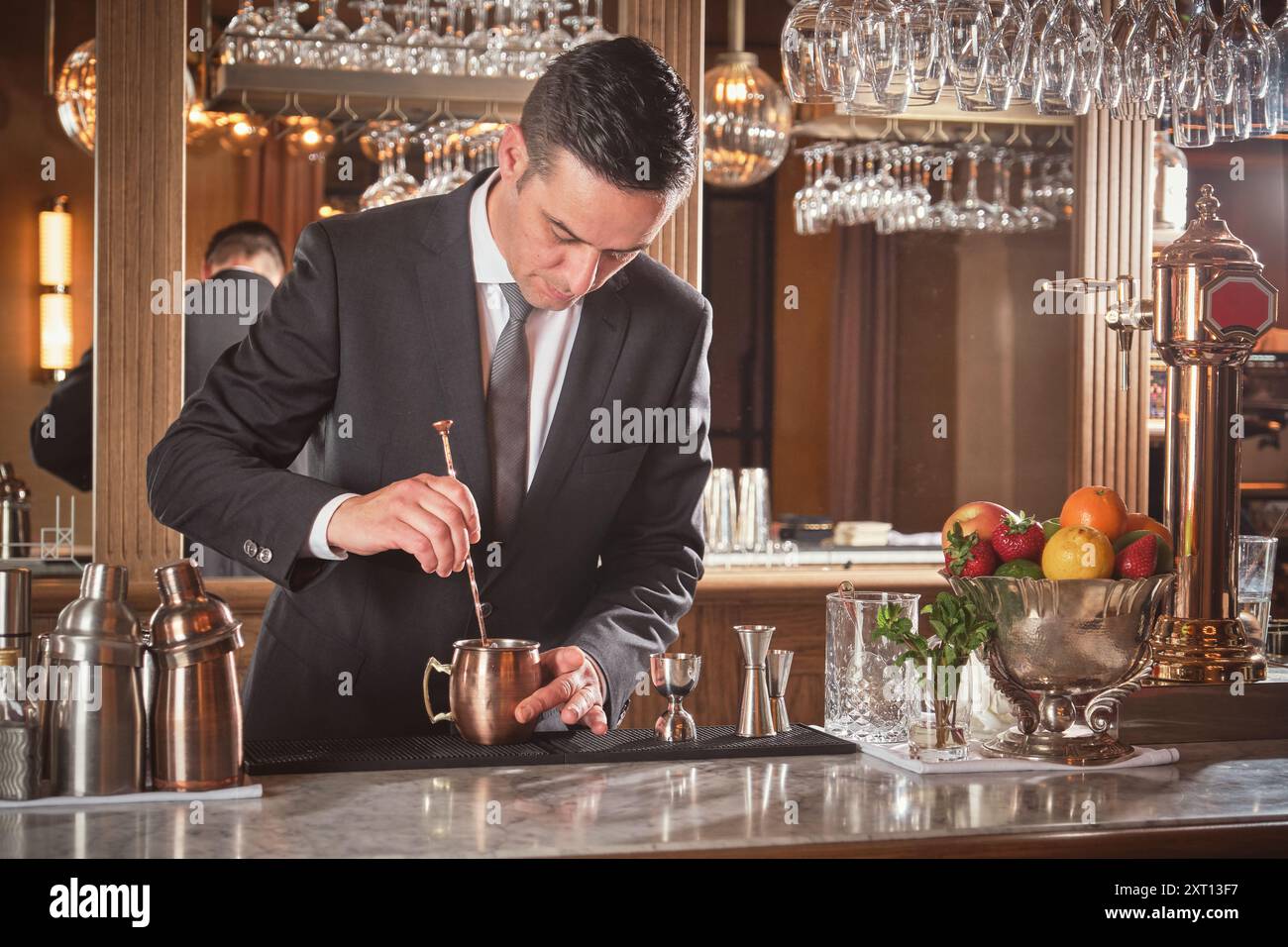 Focused barkeeper in elegant suit standing at bar counter and mixing ...