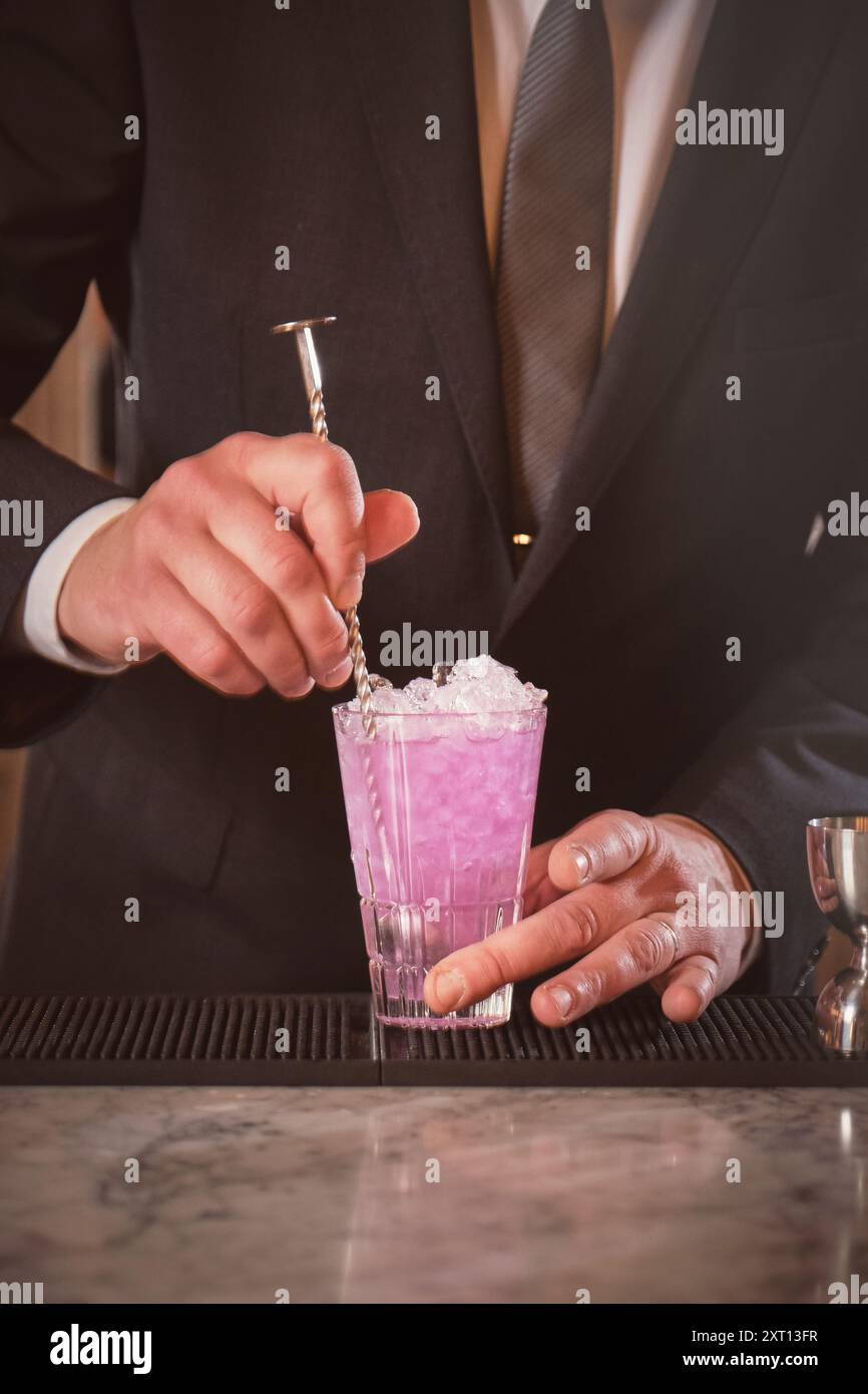 Crop anonymous male bartender in black suit mixing cocktail with spoon ...