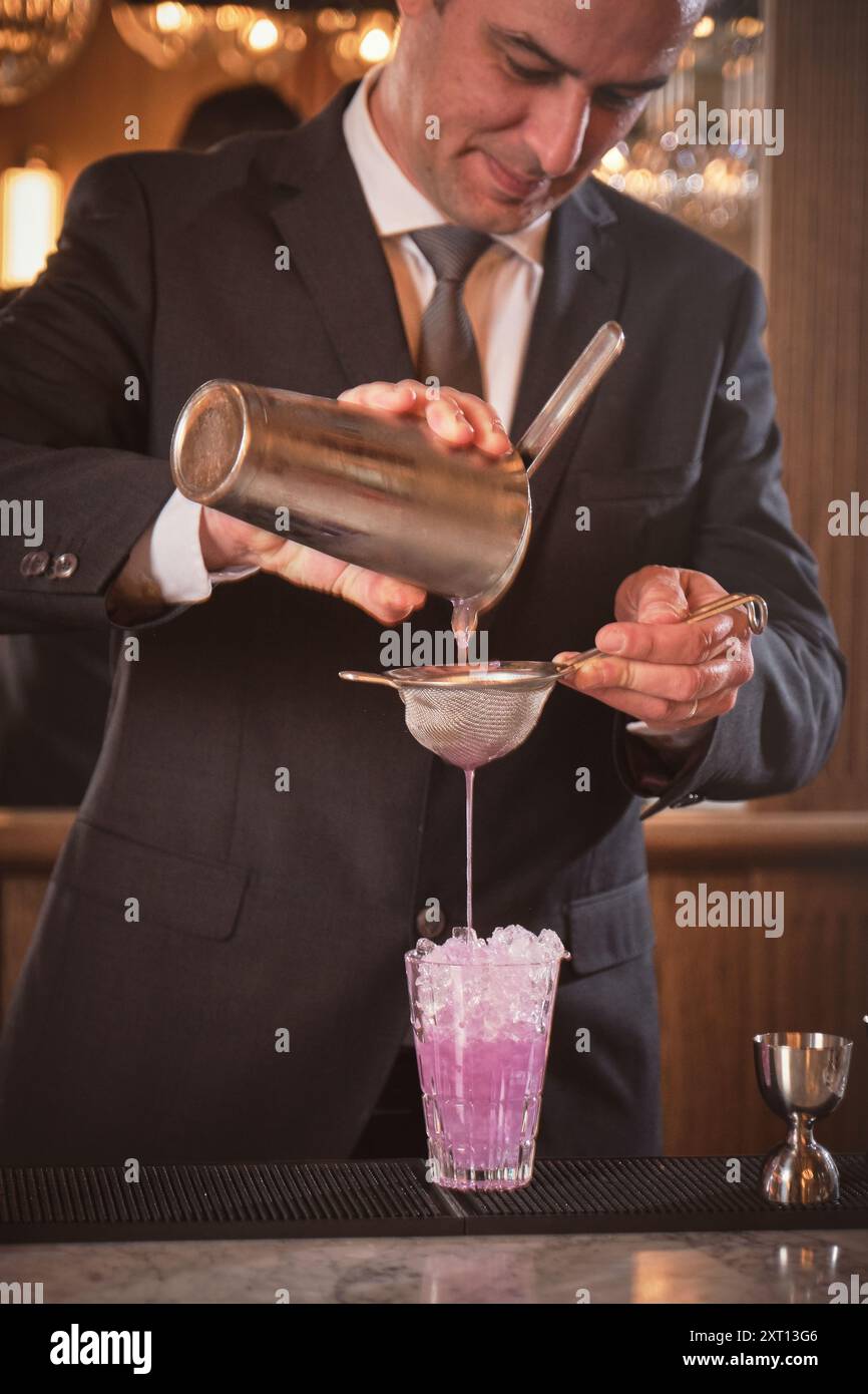 Male bartender in black suit pouring cocktail from shaker through ...