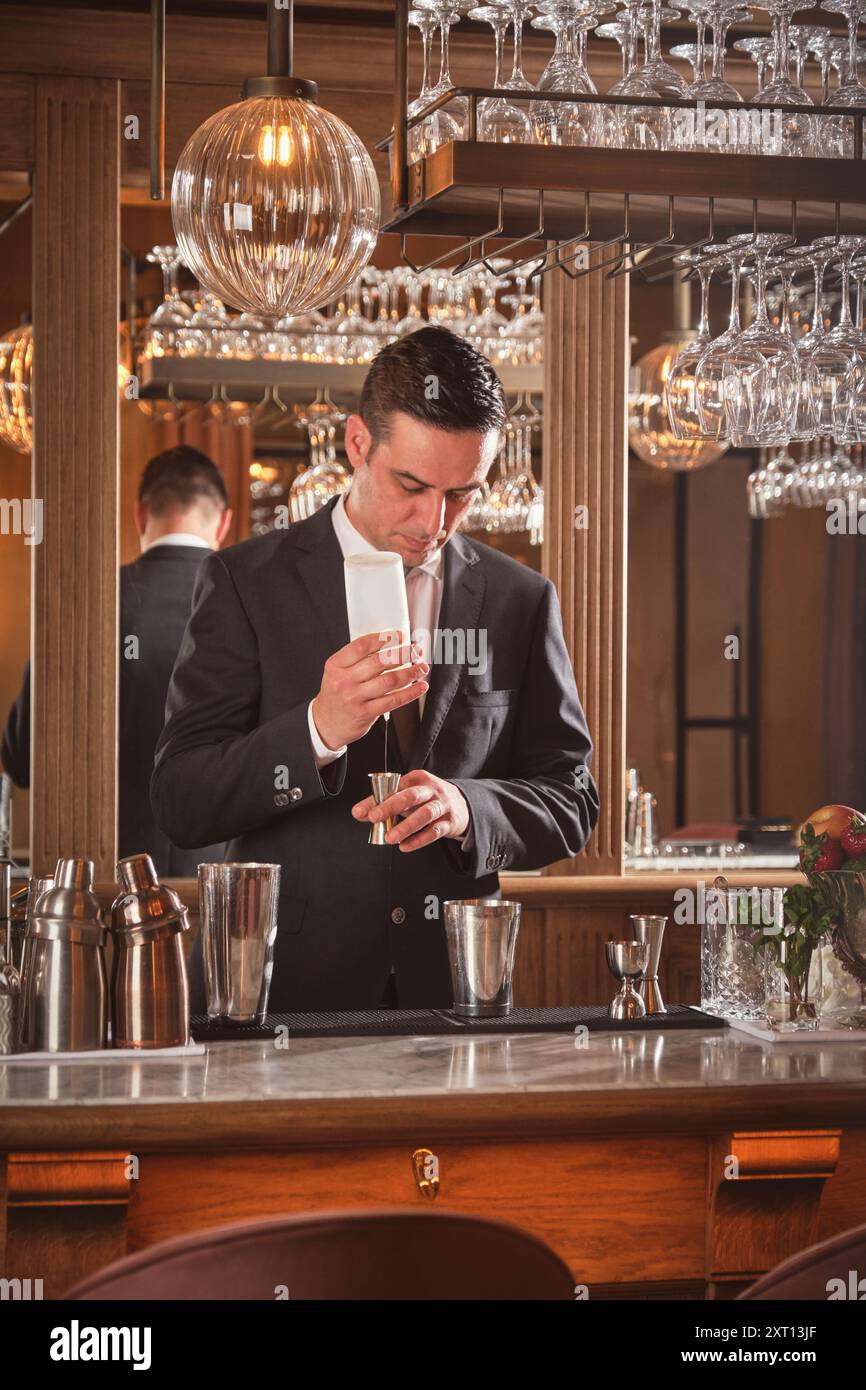 Male bartender in suit pouring syrup in measuring cup while preparing ...