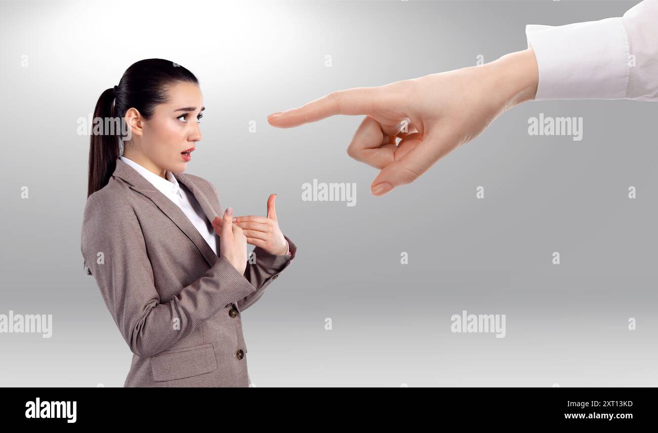 Boss or colleague pointing at confused woman on grey background ...
