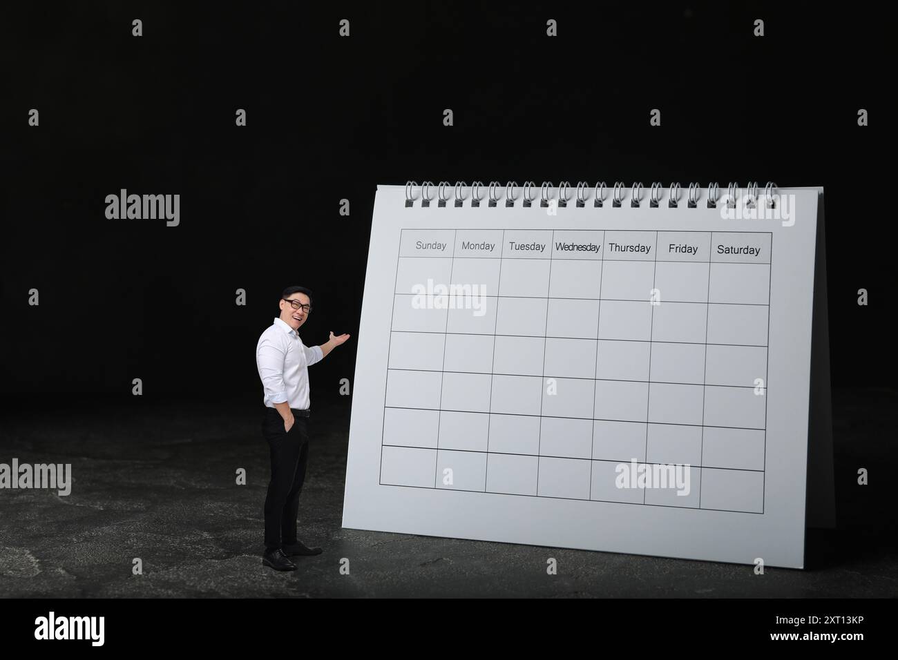 Happy small businessman pointing at big calendar on black background ...
