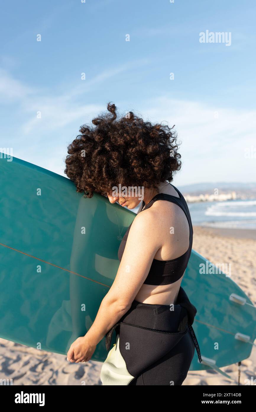 Side view of young female surfer in wetsuit with surfboard standing ...