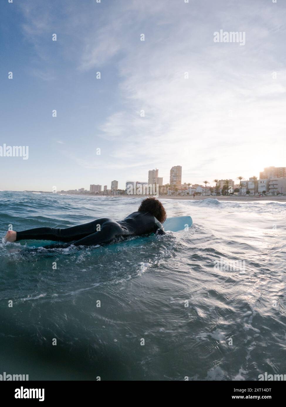 Side view of young female surfer in wetsuit lying on waving seawater ...