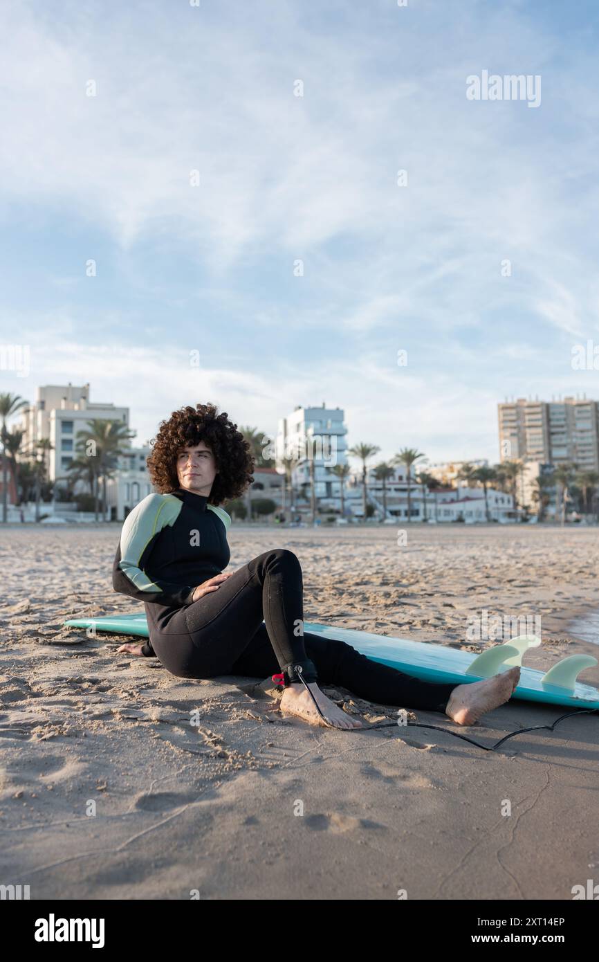 Side view full body of barefoot female surfer in wetsuit sitting on ...