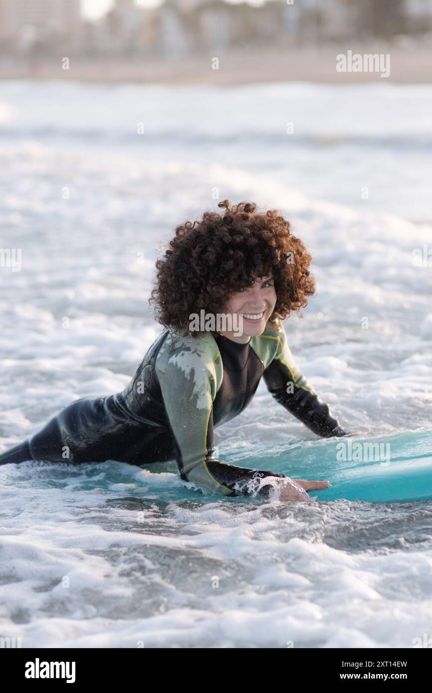 Side view of young happy female surfer in wetsuit lying on waving ...