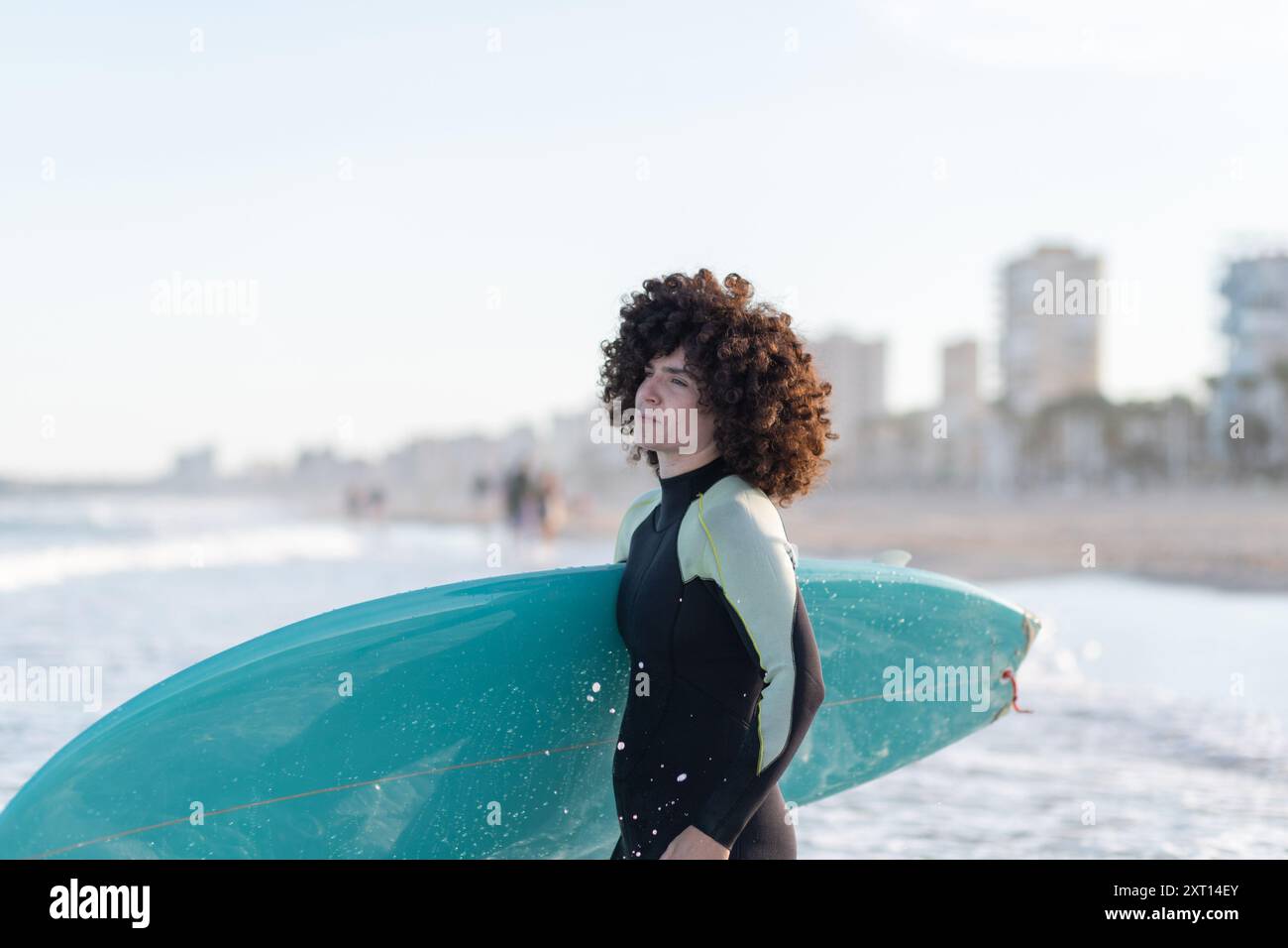 Side view of young thoughtful female surfer in wetsuit with surfboard ...