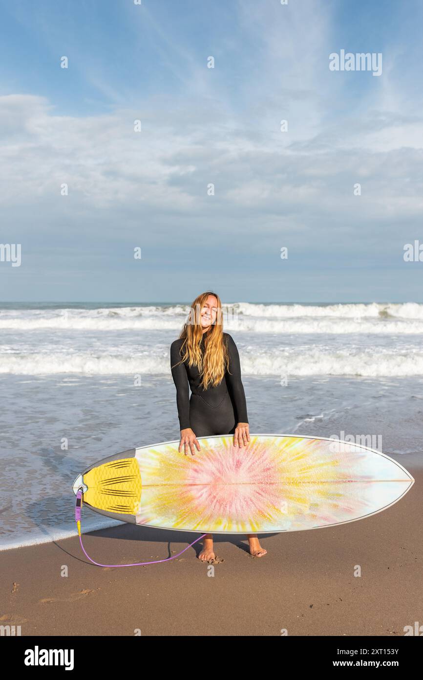 Full body of sportive female surfer in black wetsuit standing on wet ...
