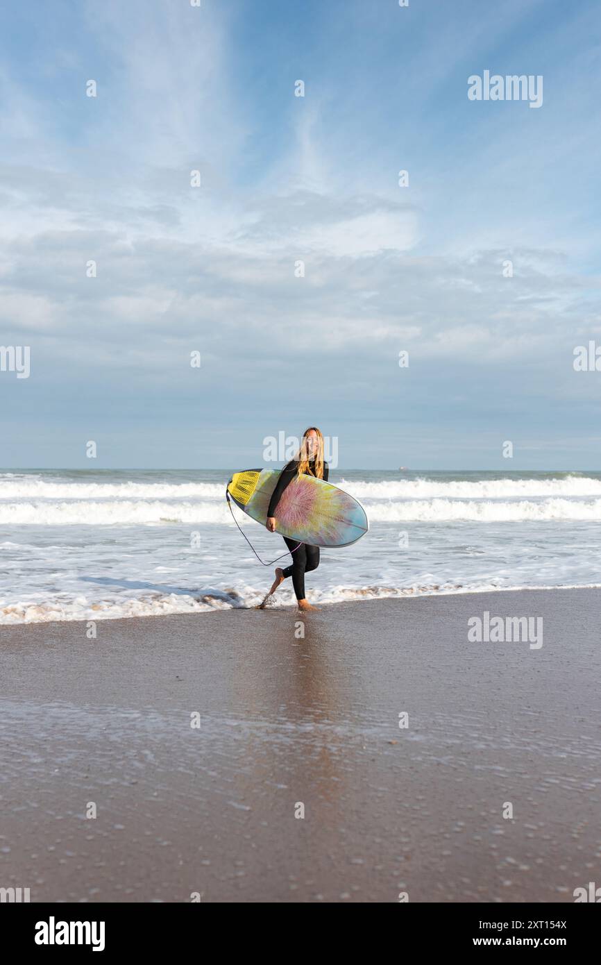 Full body side view of sportive female surfer in black wetsuit walking ...