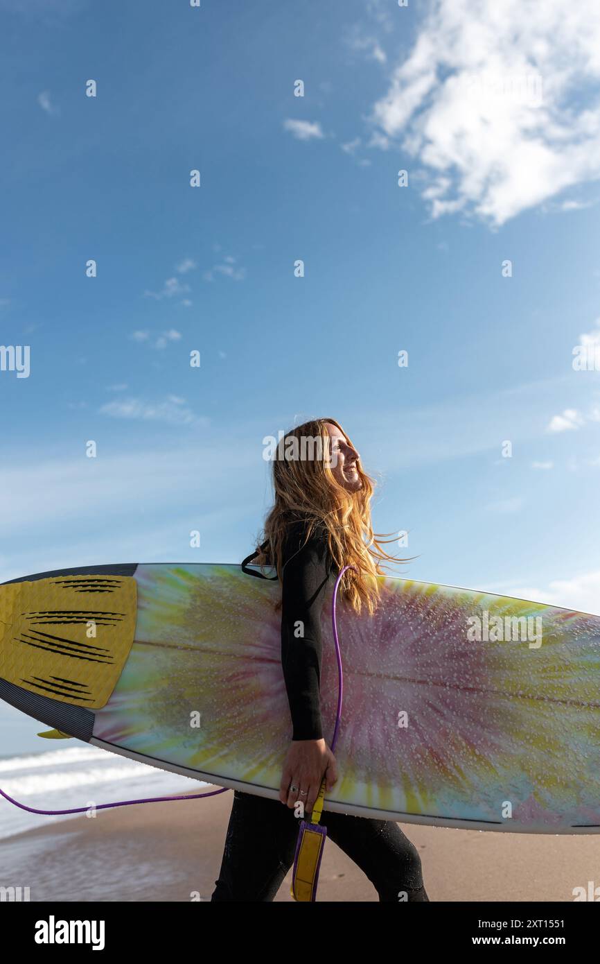 From below of sportive female surfer in black wetsuit walking on wet ...