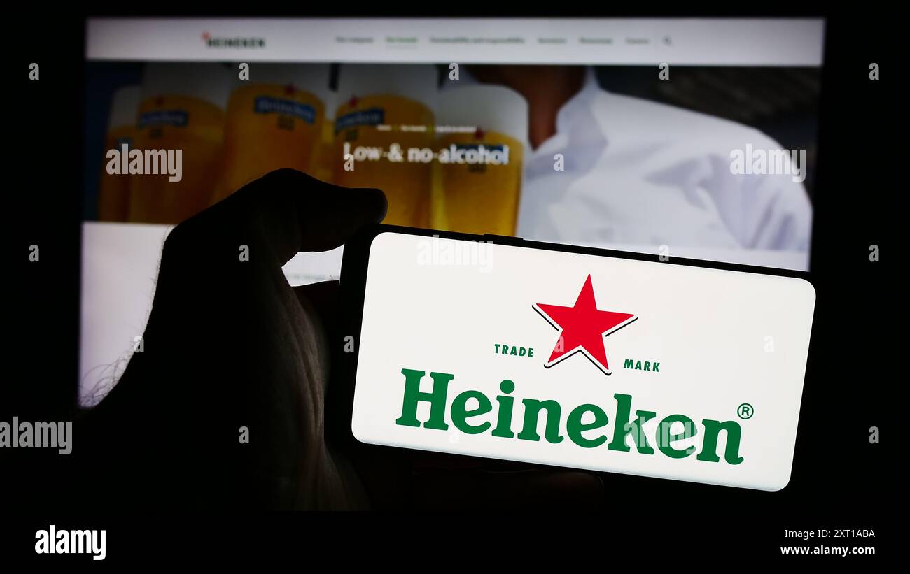 Person holding mobile phone with logo of Dutch brewing company Heineken NV in front of business ...