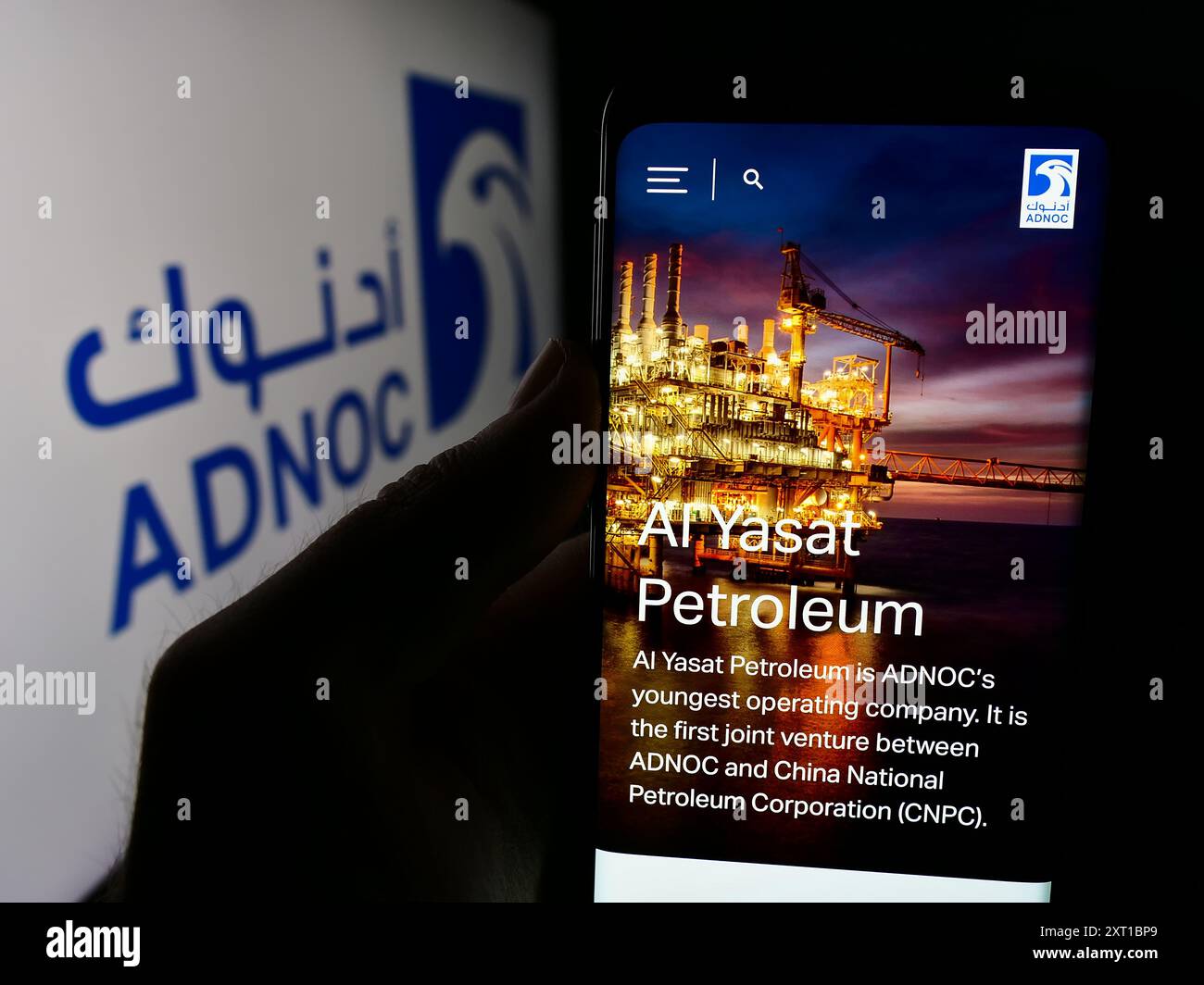 Person holding cellphone with webpage of oil business Abu Dhabi National Oil Company (ADNOC) in ...
