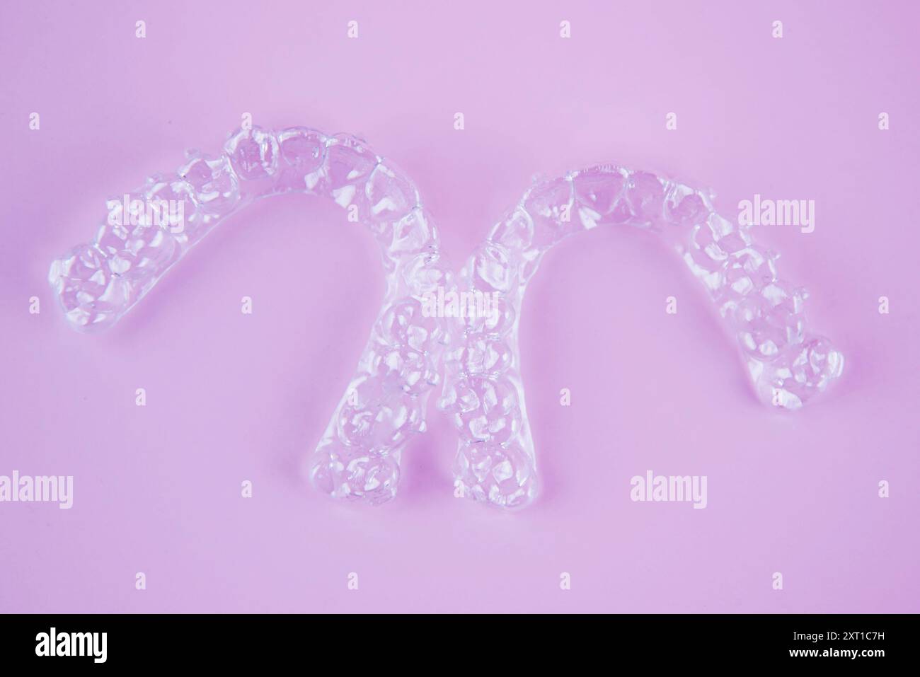 Invisible aligner teeth retainers on a pink background. Plastic dental ...