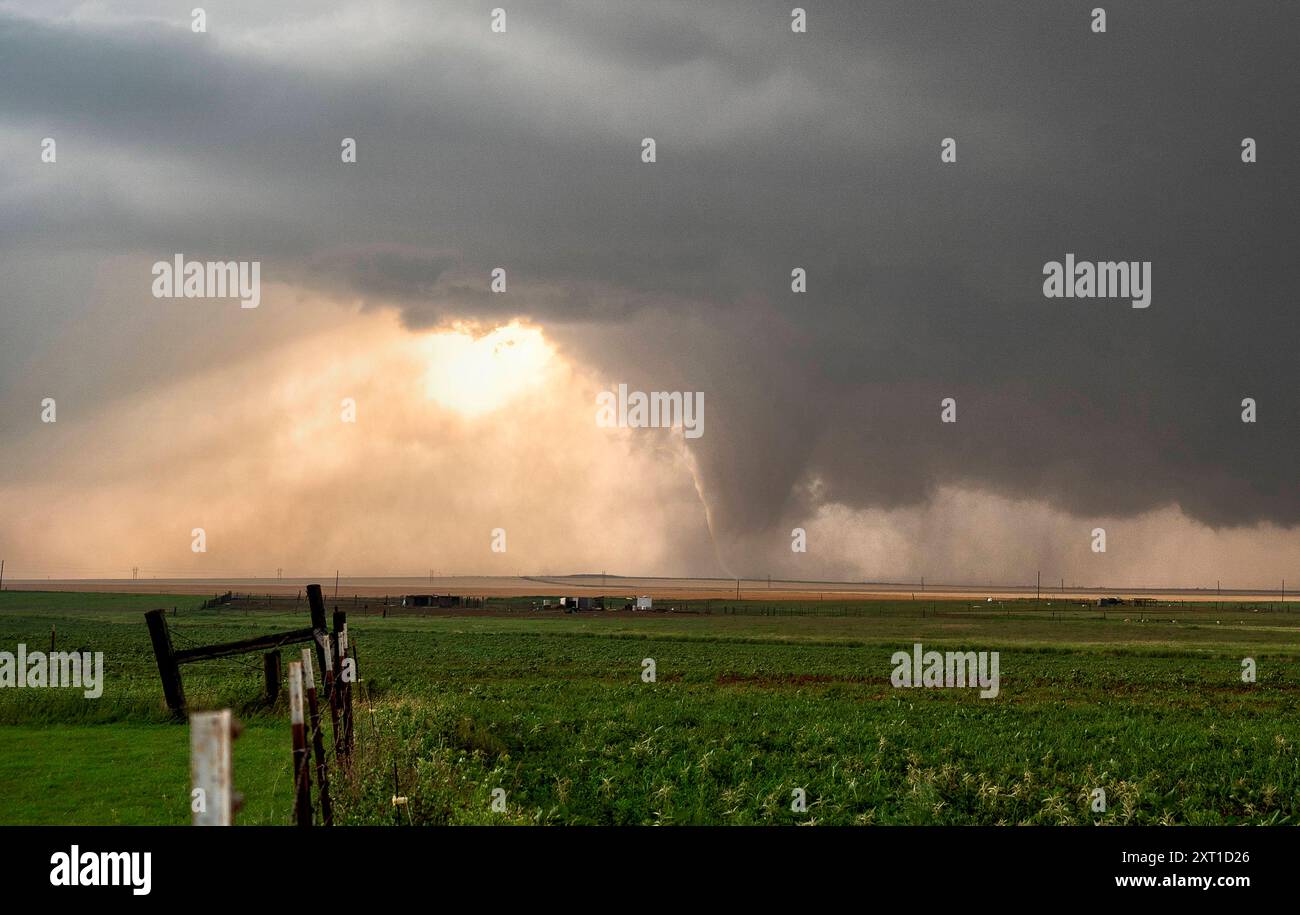 A tornado touches down in a rural area under a stormy sky, with ...