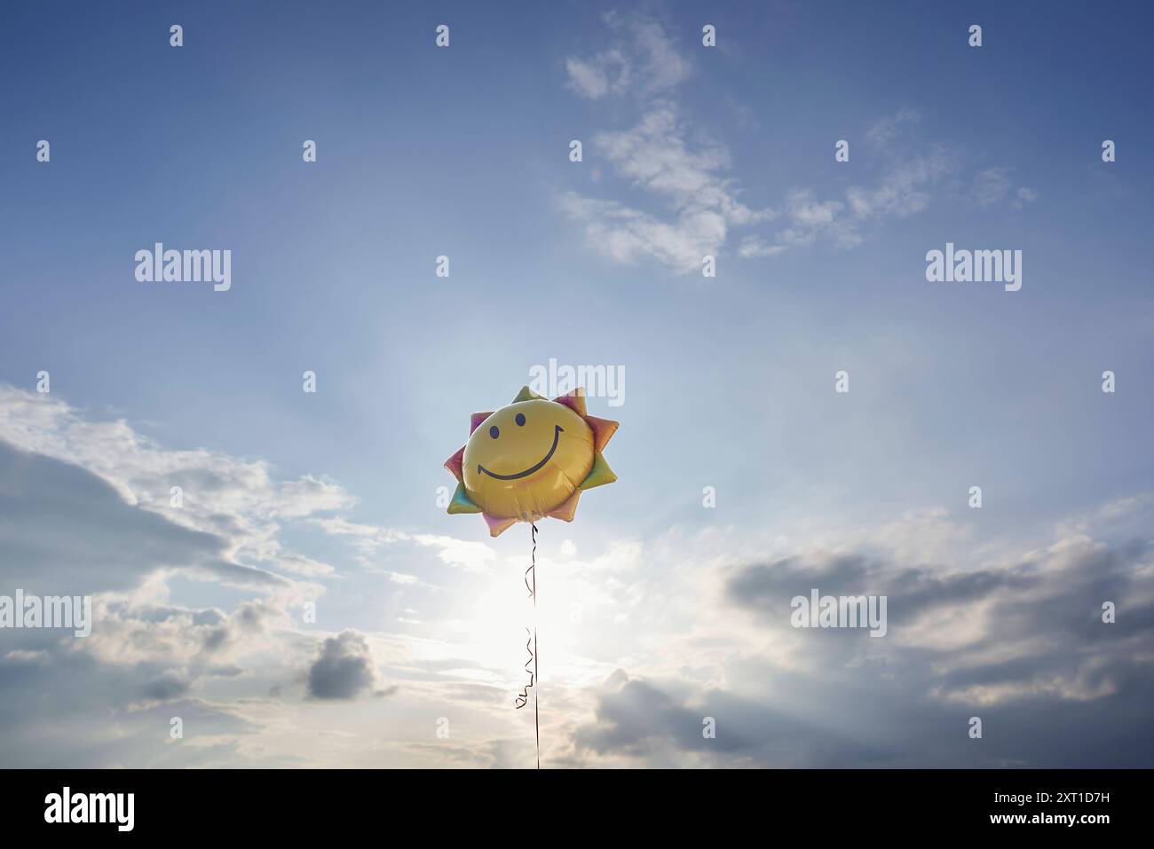 A smiling sun-shaped balloon floats against a bright blue sky with ...
