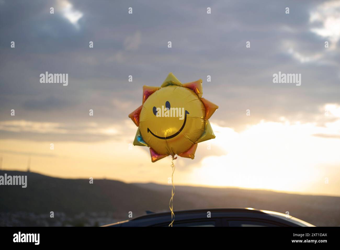 A smiling sun-shaped balloon floats in the air against a backdrop of a ...