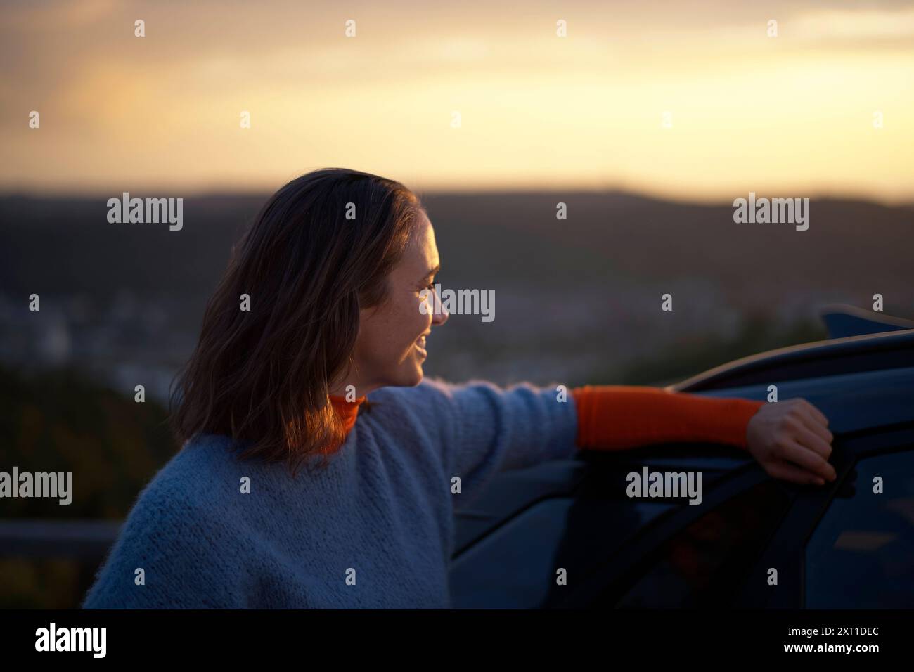 Woman enjoying sunset next to her car on a scenic overlook with a view ...