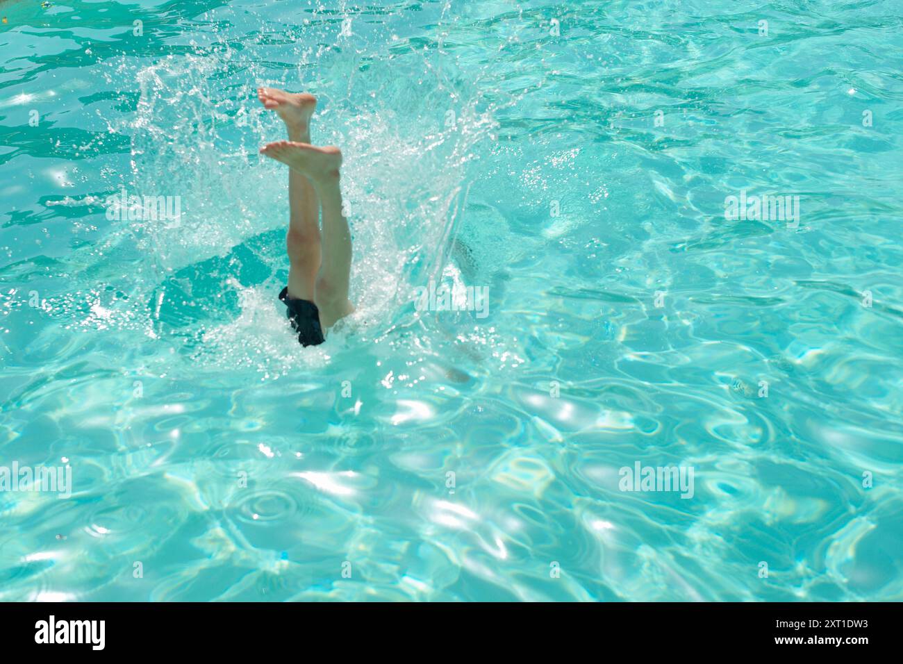Legs submerged upside down in a clear turquoise pool creating a splash ...
