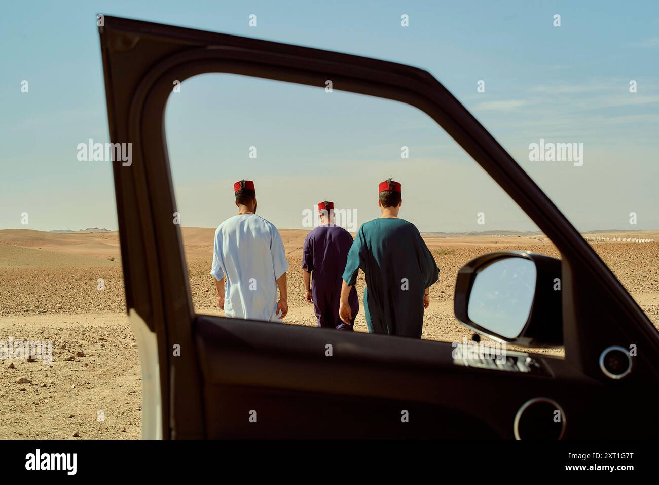 Three men in traditional attire walk through a desert landscape, viewed ...