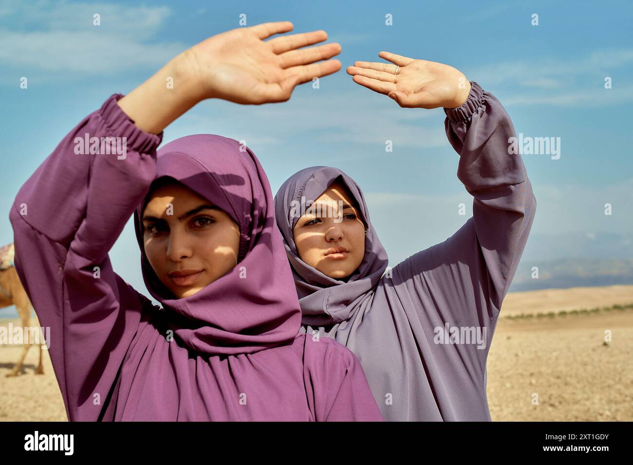 Two women in hijabs posing with their hands framing the sky in a desert landscape. bola02559 ...