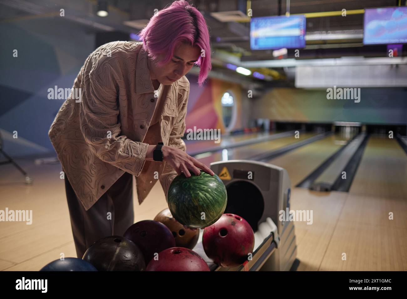 Person with pink hair in bowling alley selecting bowling ball from rack ...