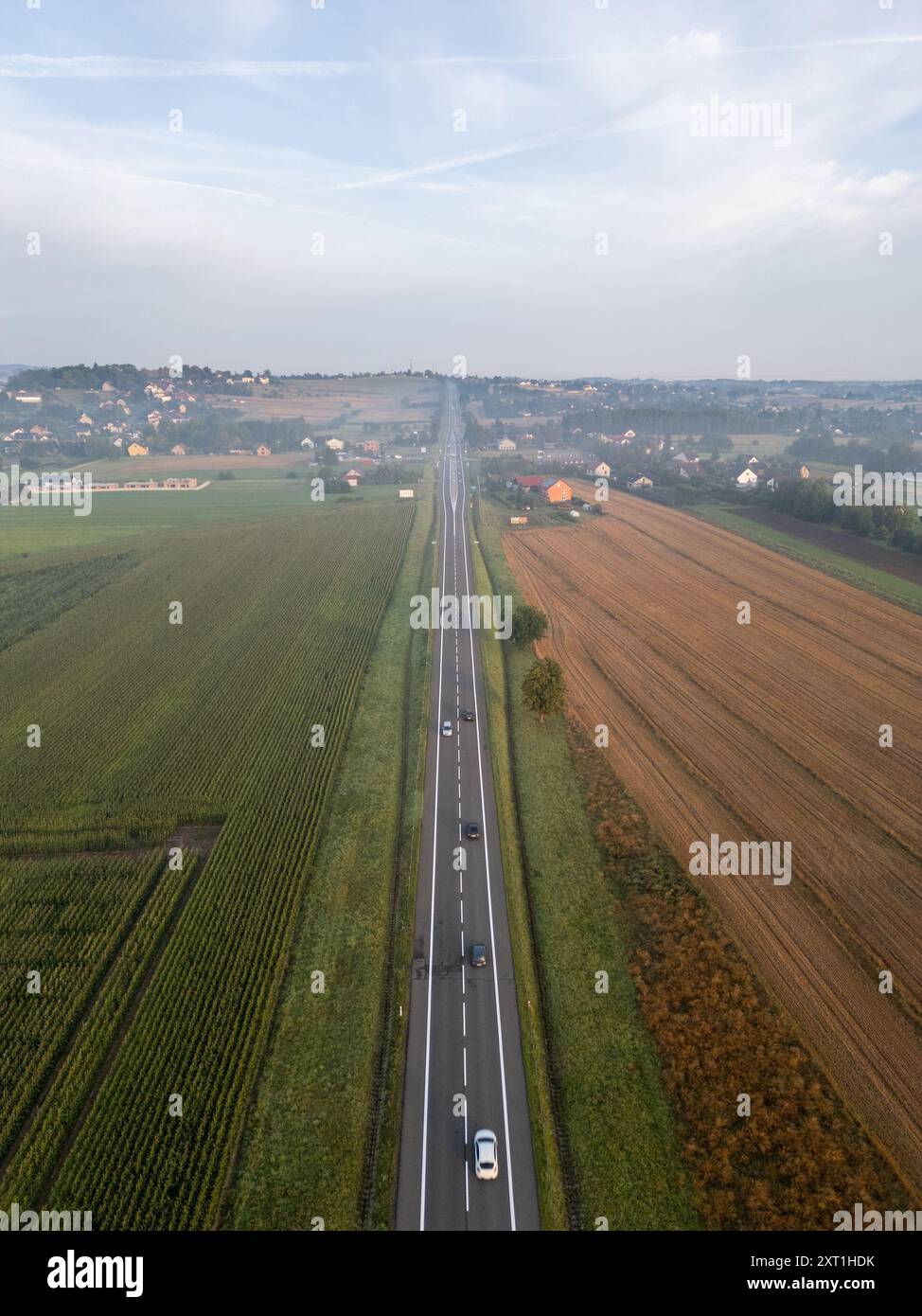 An aerial view of a long road through farmland with cars driving and a ...
