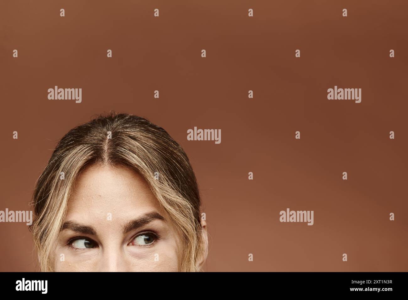 A confident young woman looks off-camera against a warm beige backdrop ...