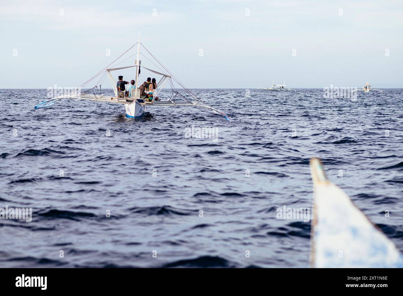 Traditional outrigger canoe sailing across the open sea with people ...