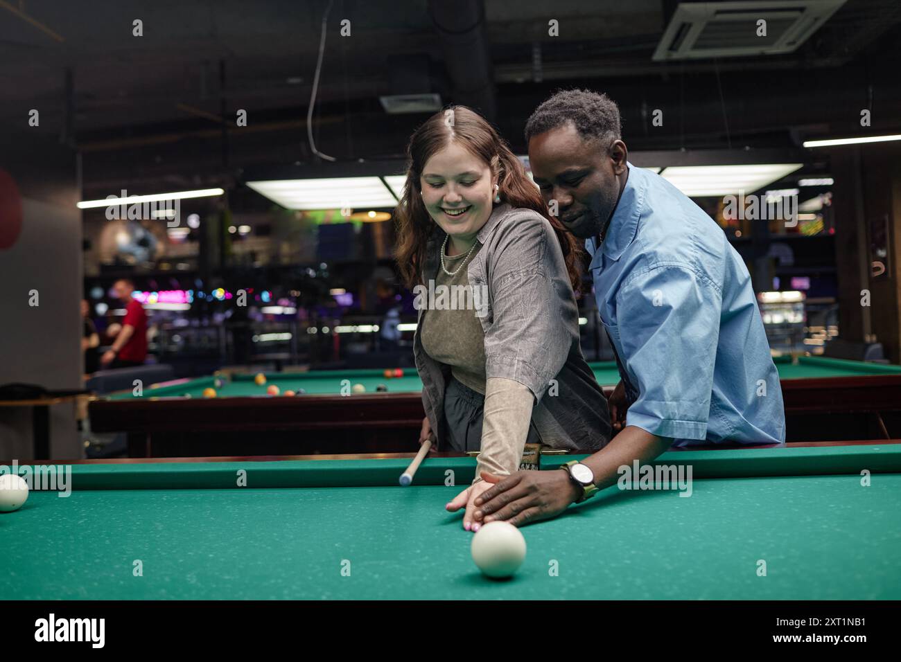 Man assisting woman learning billiard skills on pool table with pool ...