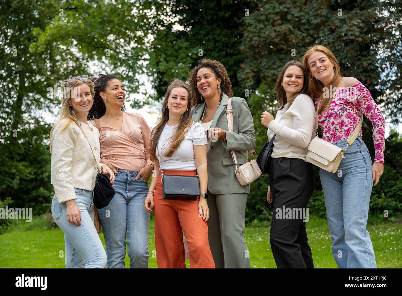 Group of joyful women friends posing together in a park with greenery ...