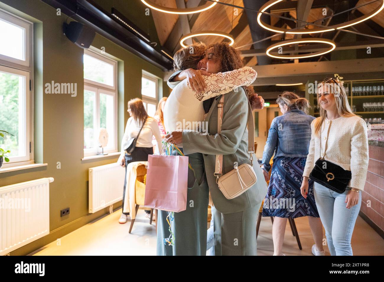 Two friends hug warmly in a cozy cafe while another woman looks on with ...