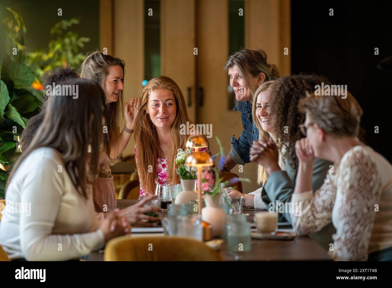 A group of joyful women engaging in conversation around a dining table ...