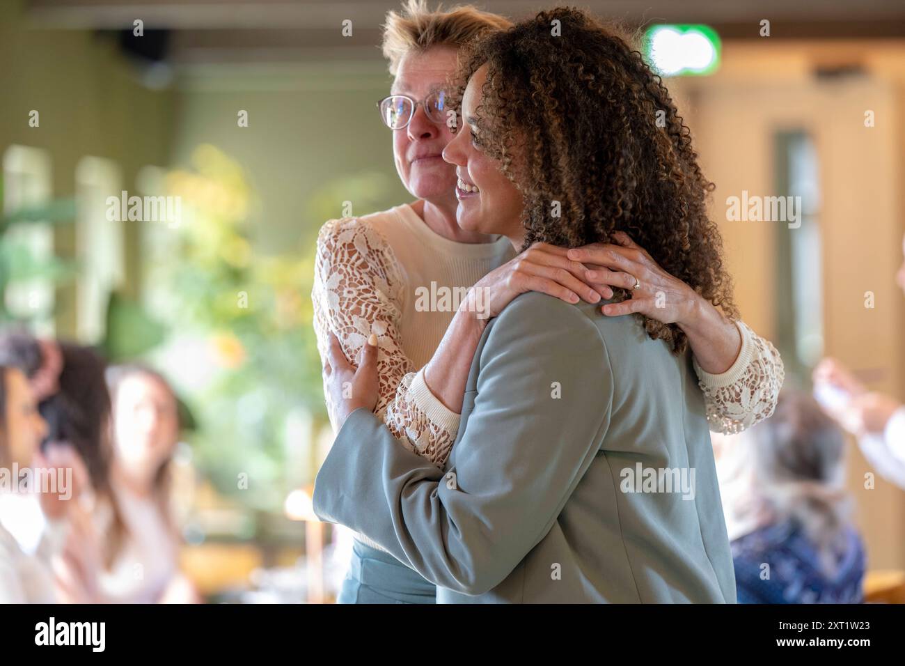 Elderly woman with glasses embracing a younger woman with curly hair ...